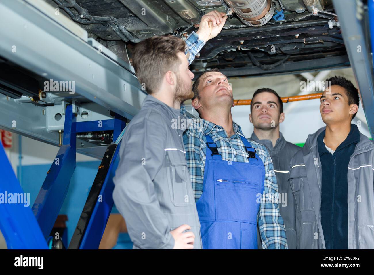 apprentice mechanics looking at car raised on hydraulic lift Stock ...