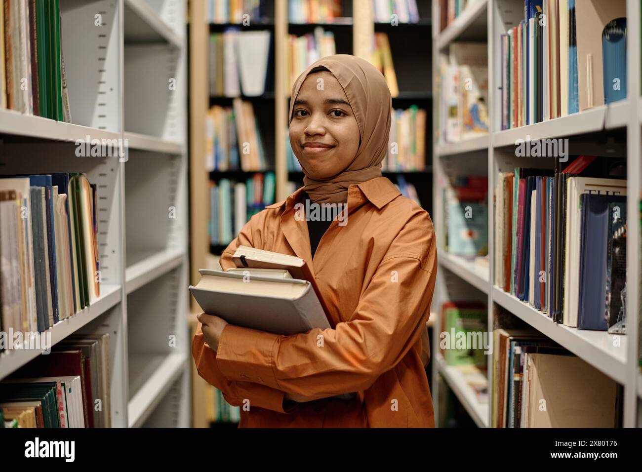 Medium portrait of joyful Muslim girl wearing hijab holding books ...