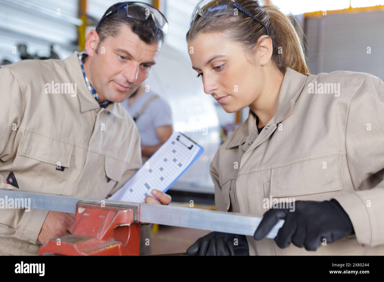 foreman watching female worker clamp metal into vice Stock Photo - Alamy