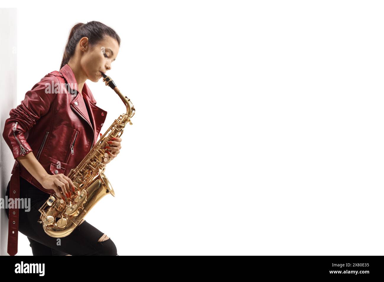 Young woman in a leather jacket playing a sax and leaning on a wall ...
