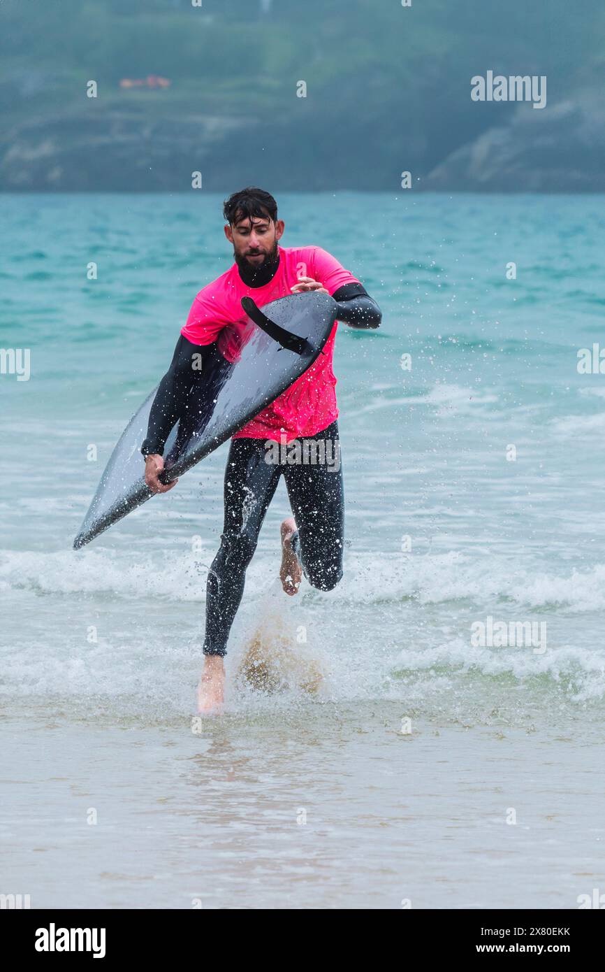 A surfer carrying his surfboard and running out of the sea during the ...