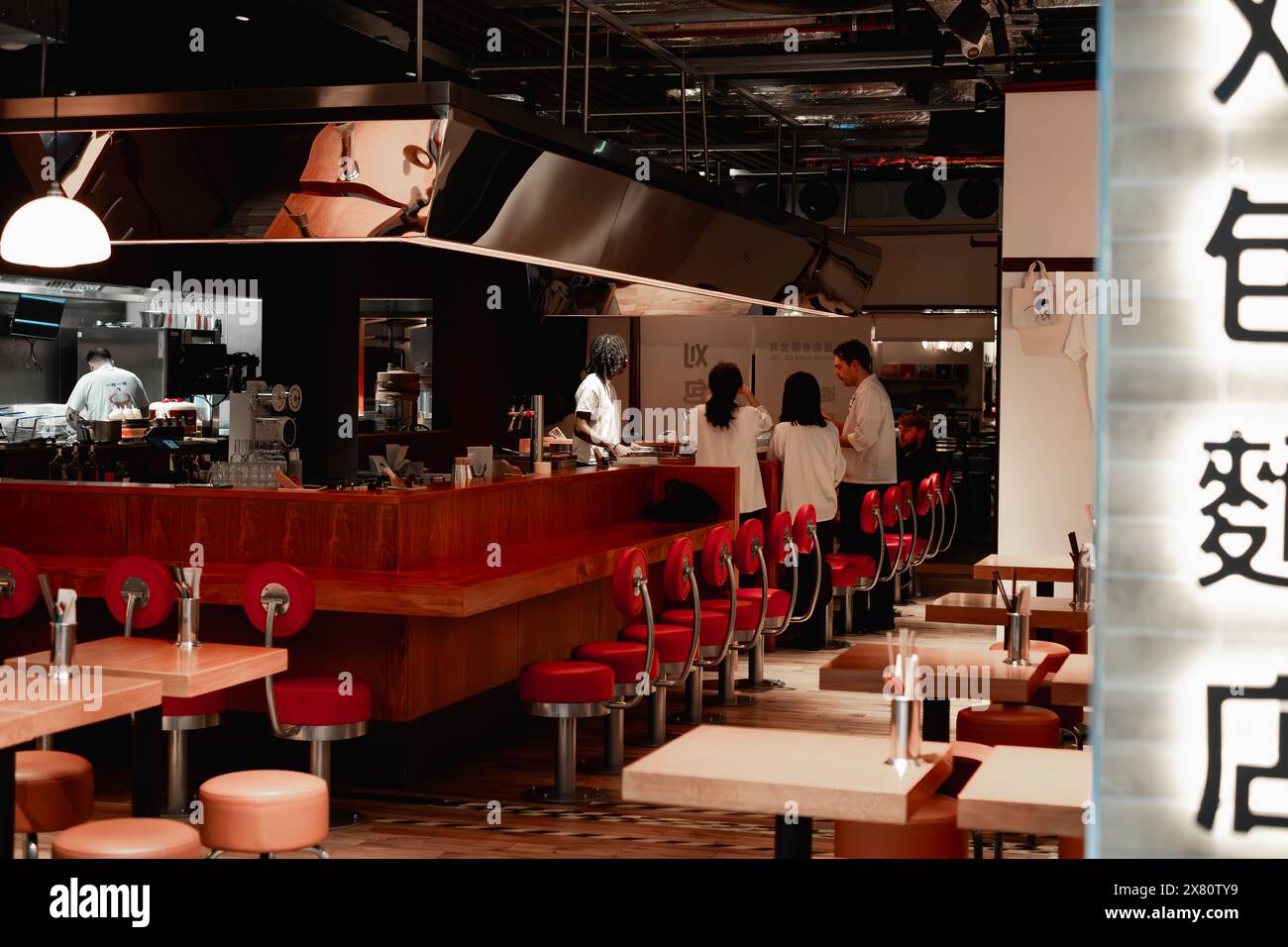 Group of 4 chefs in a meeting in a restaurant with another chef cooking ...