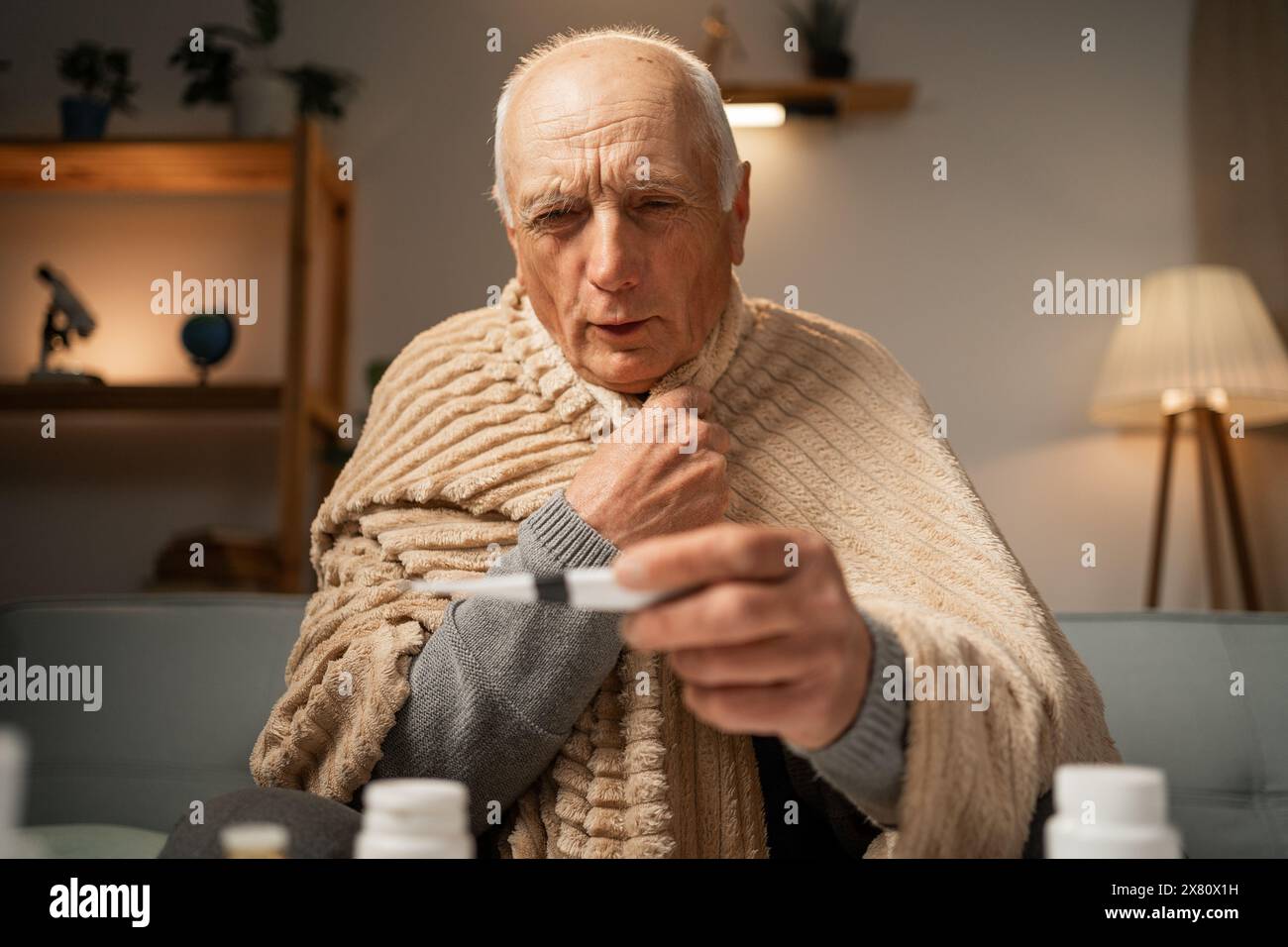 elderly, unhealthy man, measuring his temperature, holds thermometer in ...