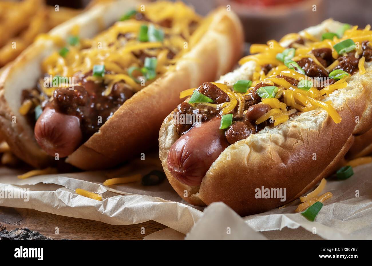 Closeup of two chili hot dogs with shredded cheddar cheese and chopped ...