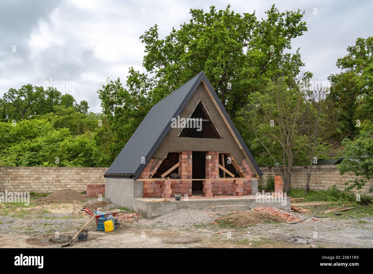 A small house with a brick wall and roof is being built. The roof has a ...