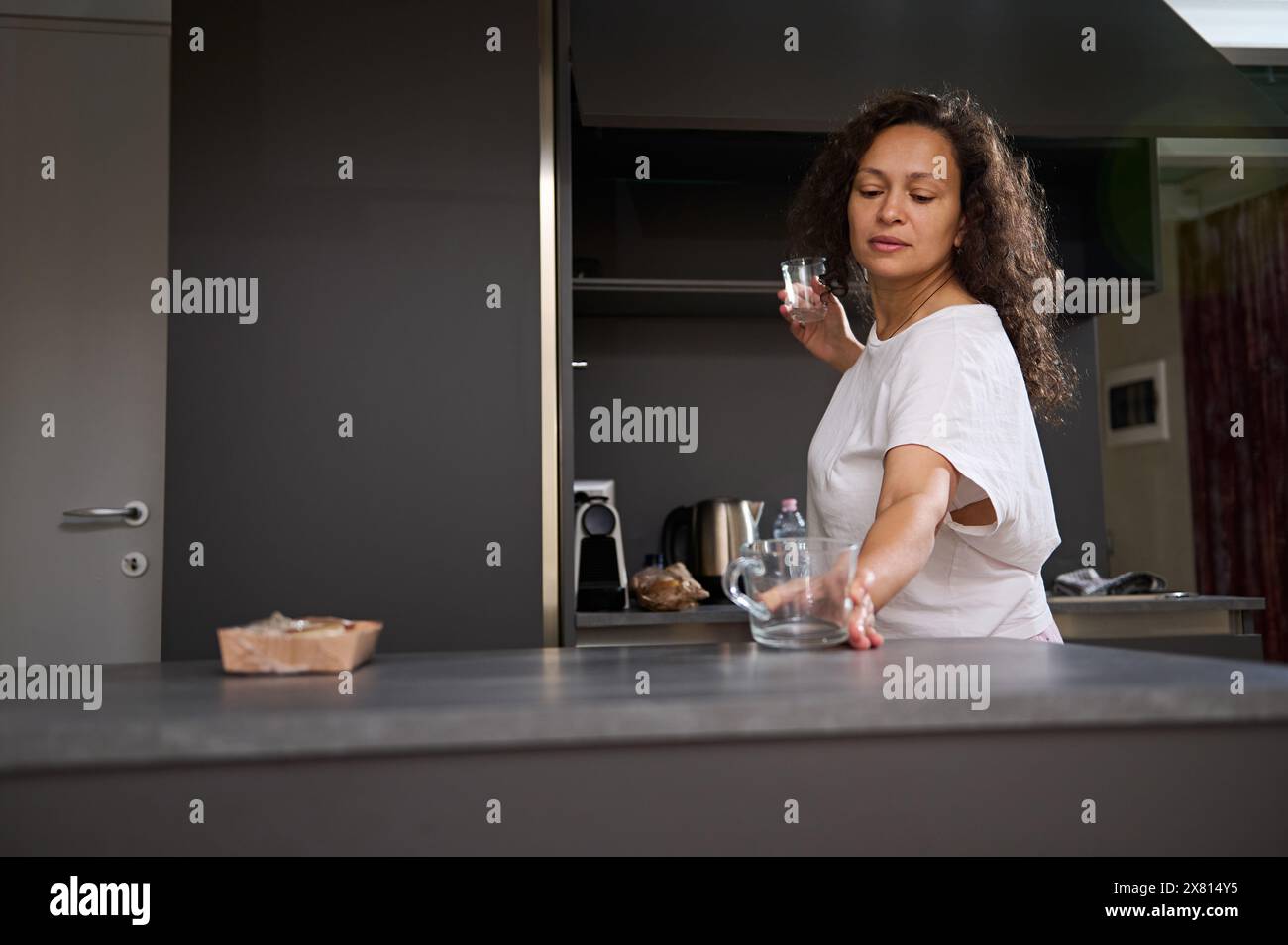Multi ethnic young pretty woman taking out a glass cup from a cupboard ...