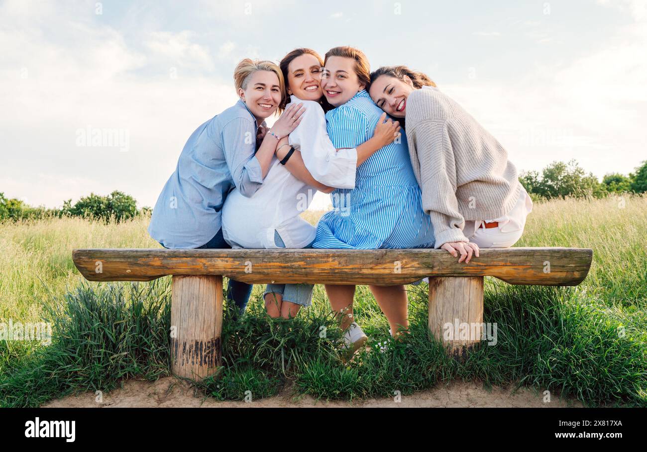 Four smiling women dressed light summer clothes harm embracing sitting ...