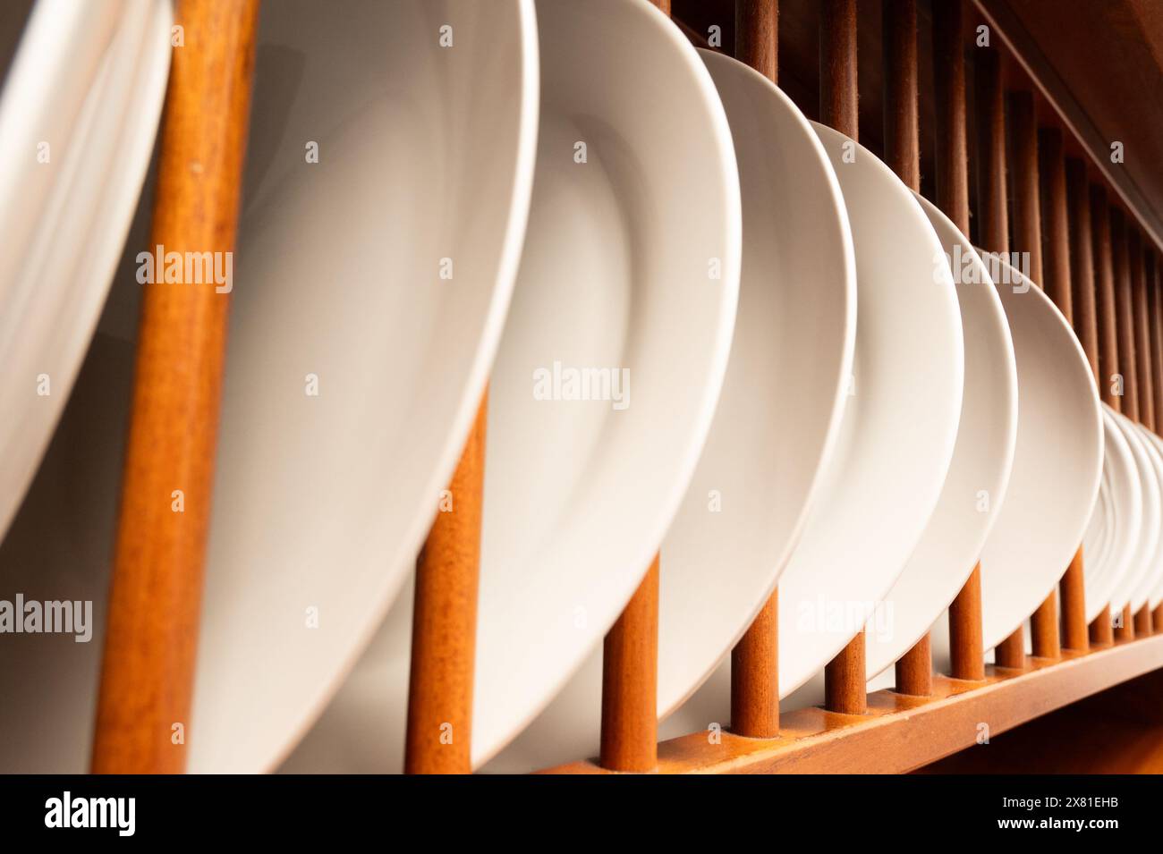 A wooden rack with many white plates on it. The plates are stacked in a ...
