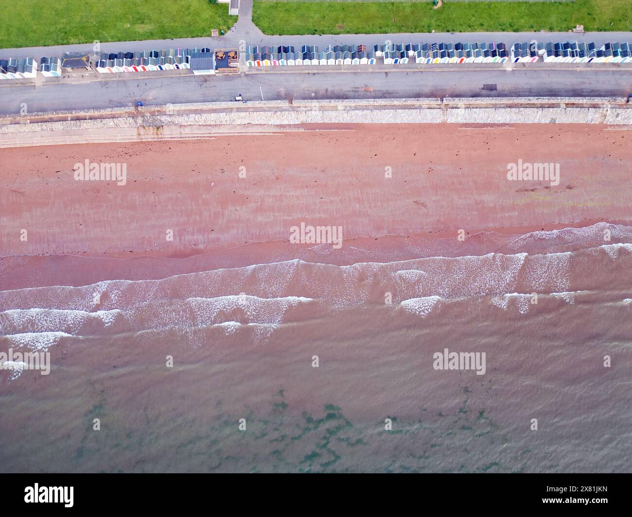 Aerial image of a long line of beach huts on a sandy beach as the waves ...
