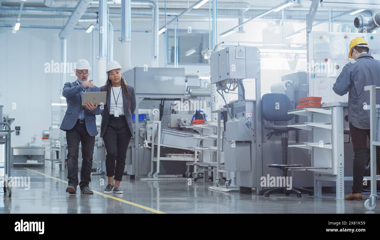 Two Diverse Heavy Industry Engineers in Hard Hats Walking with Laptop ...