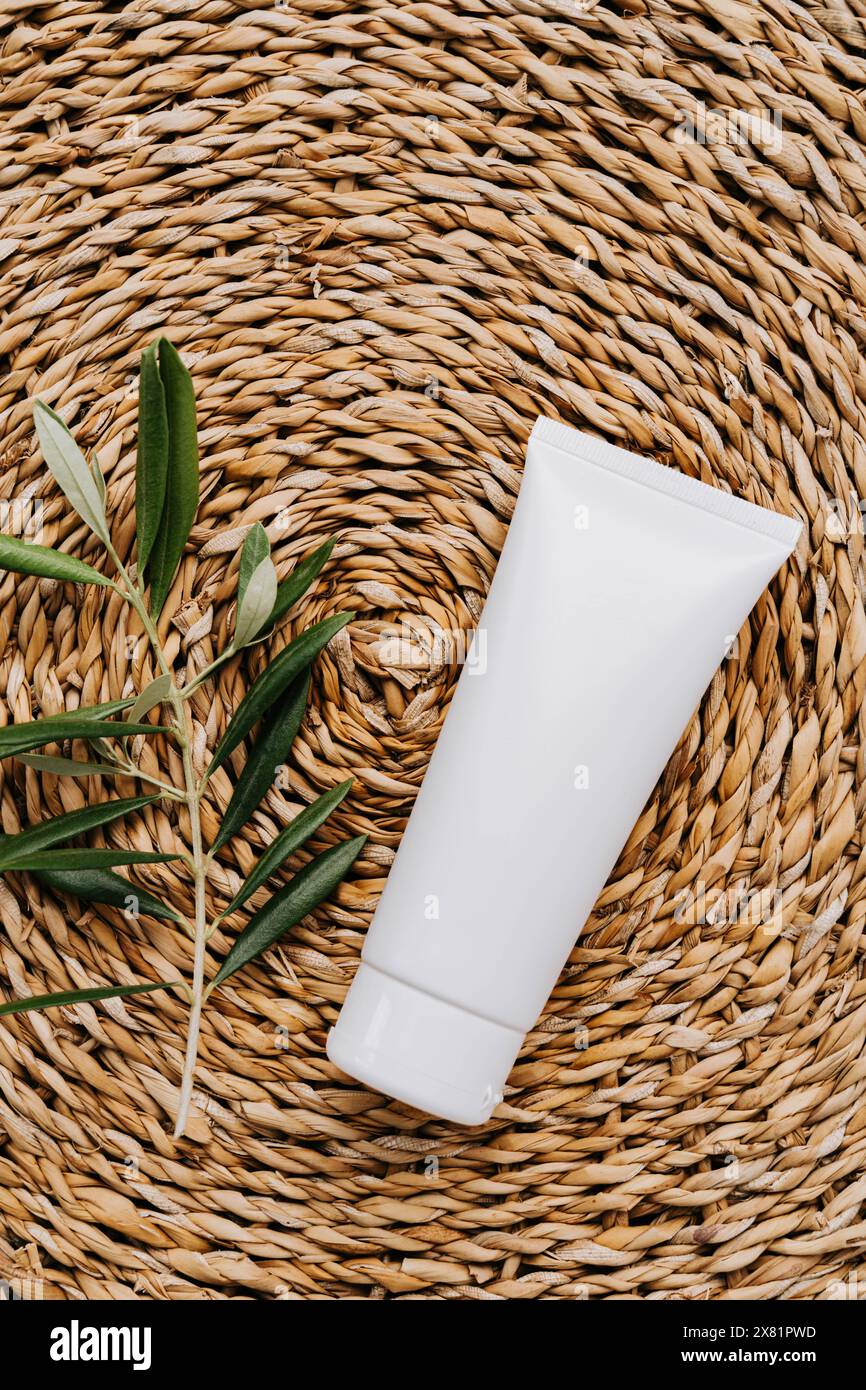 Top view of white plastic tube without label and olive branch on wicker ...