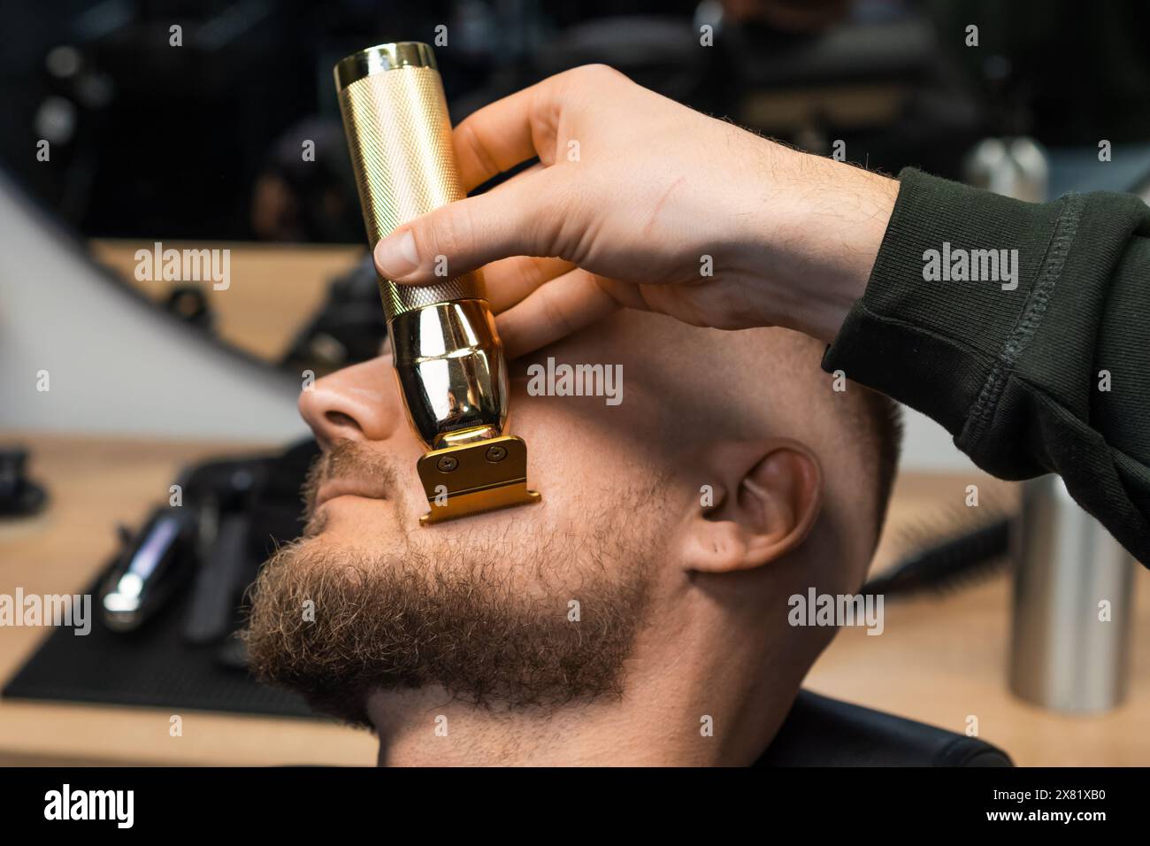 Barber trims the beard on the clients cheek, using the trimmer to ...