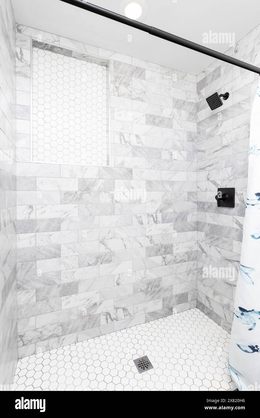 A bathroom shower with marble subway tile walls, black shower head and ...