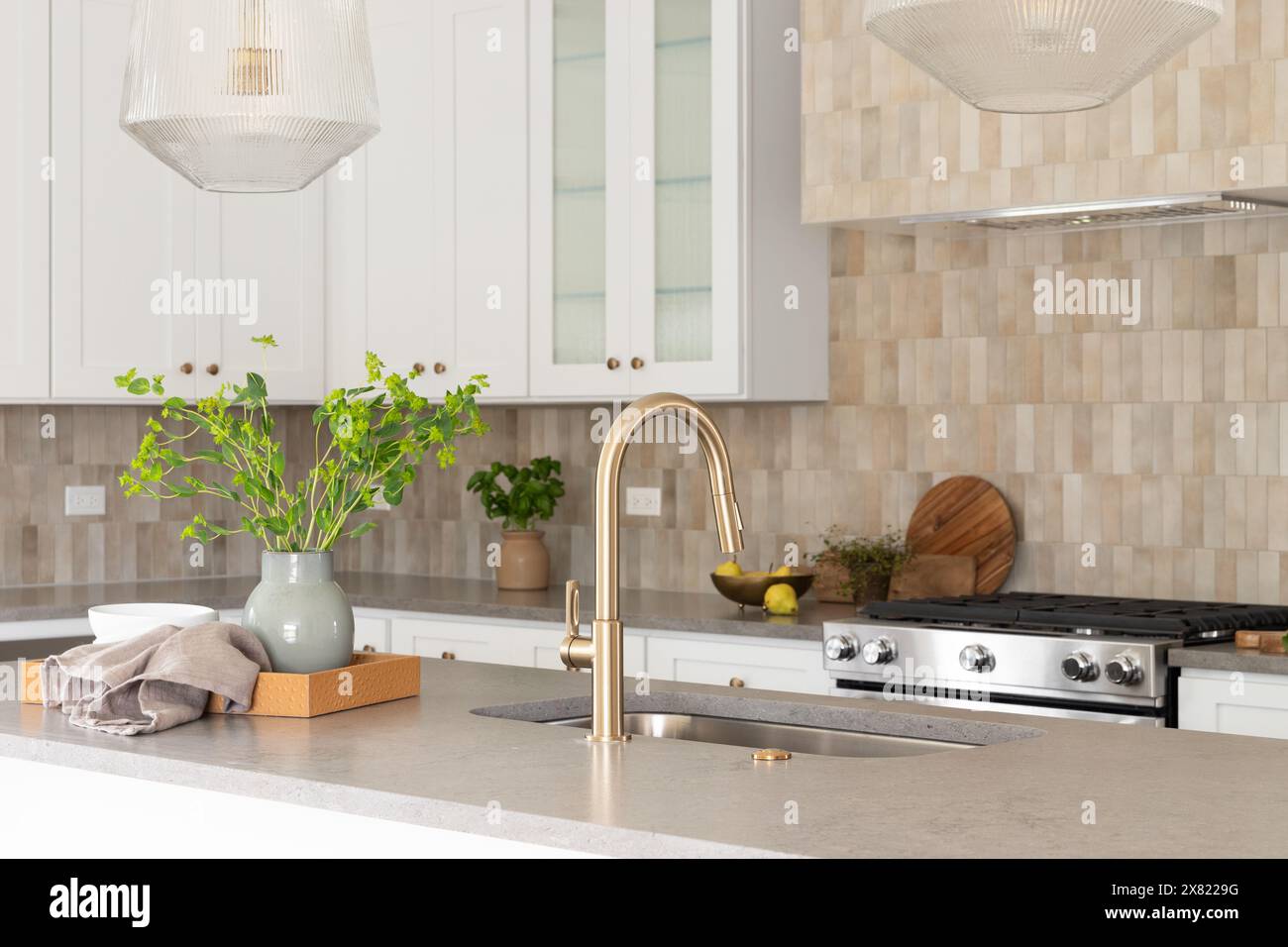 A kitchen faucet detail with a grey stone countertop island, gold ...