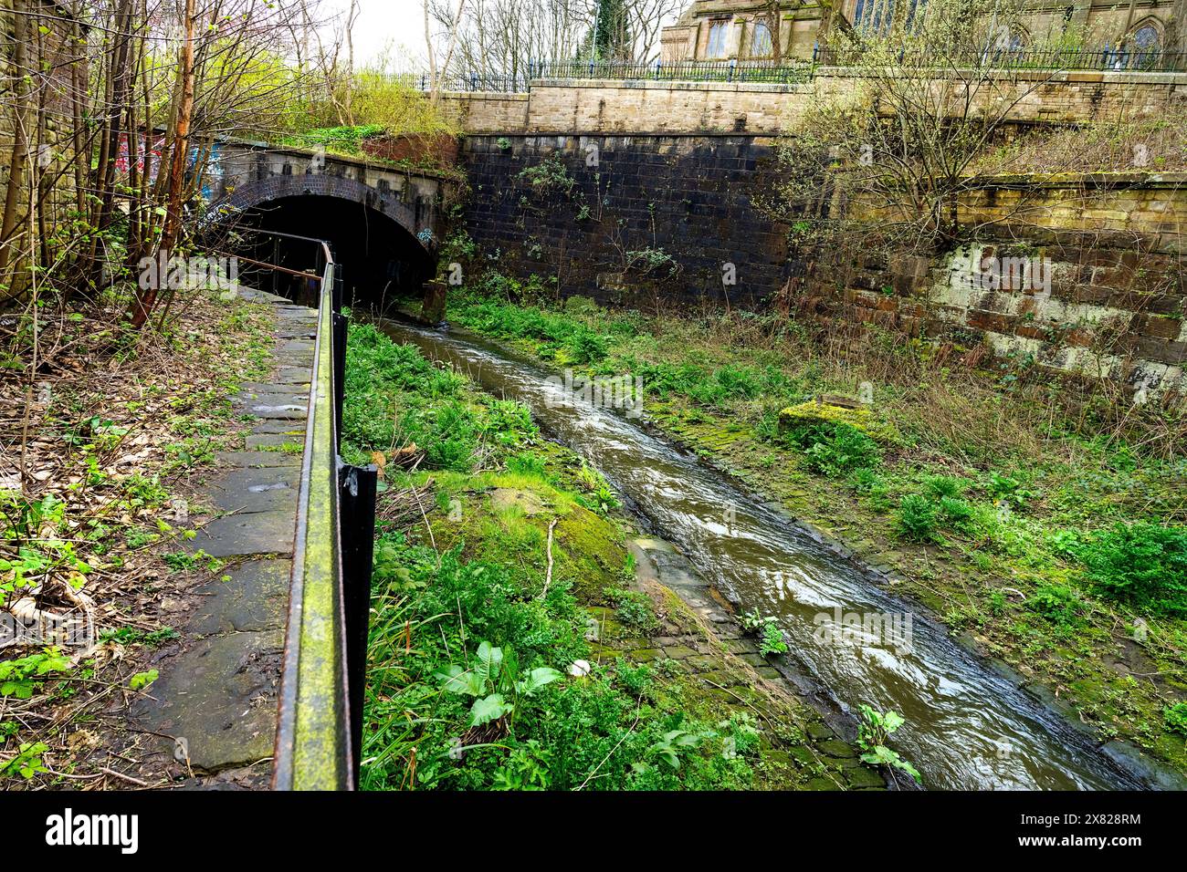 A narrow stream flows under a stone bridge surrounded by lush greenery ...