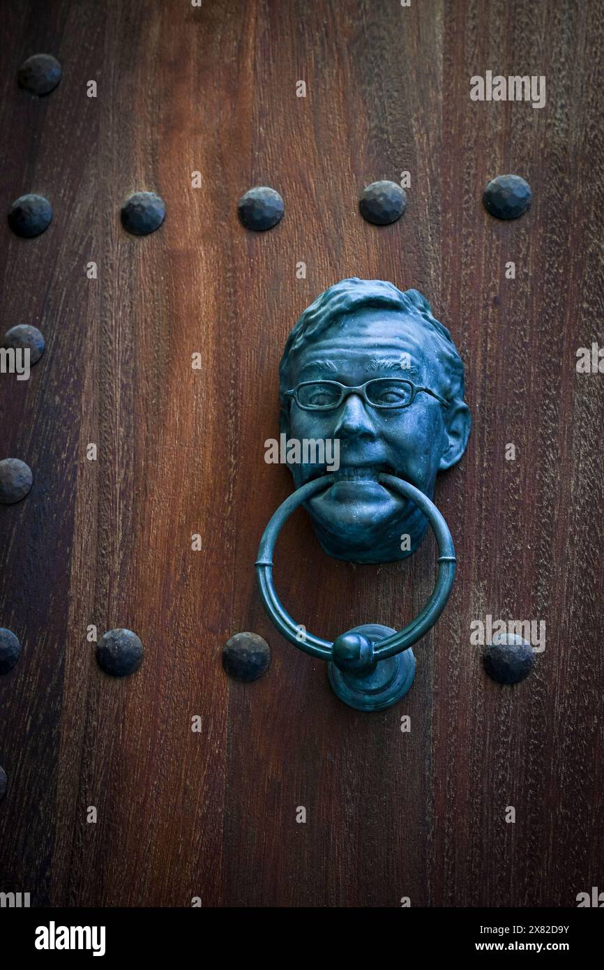 Bronze door knocker of human head with glasses, mounted on wooden door ...