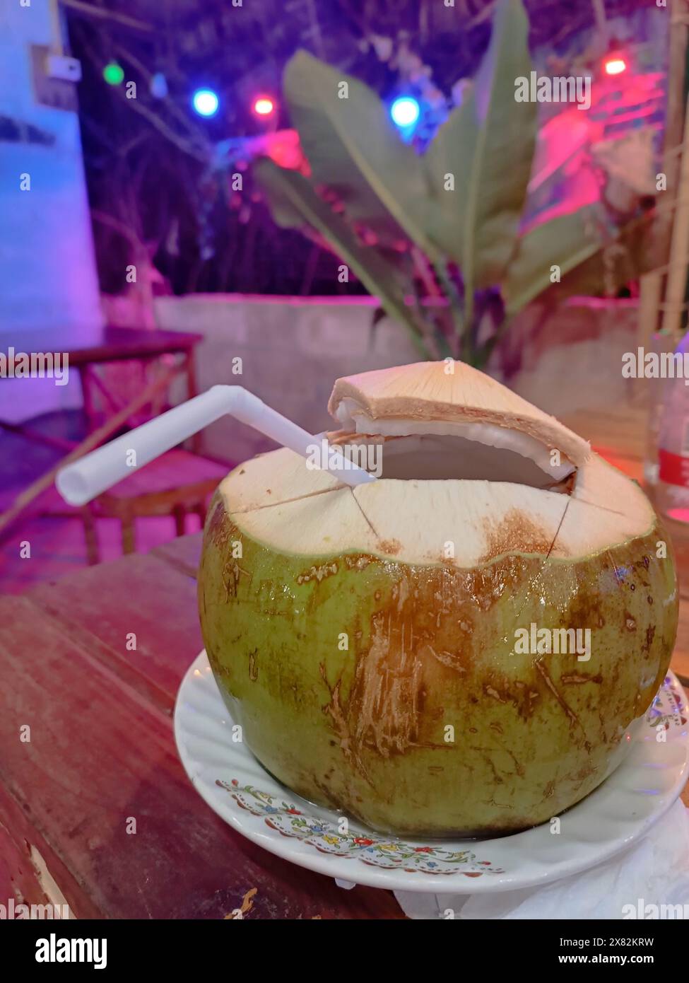 Open coconut with a straw on the table. Refreshing drink on the street ...