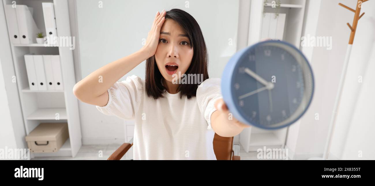 Shocked Asian woman with alarm clock in office Stock Photo - Alamy