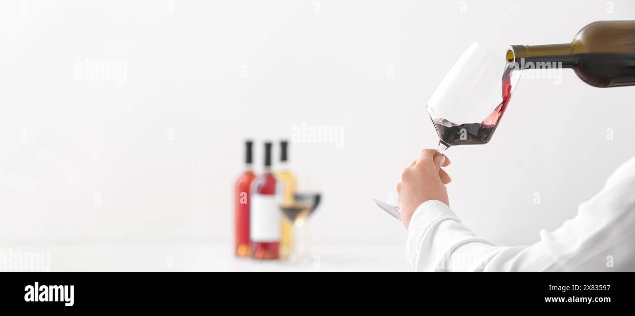 Sommelier pouring red wine from bottle into glass on light background ...
