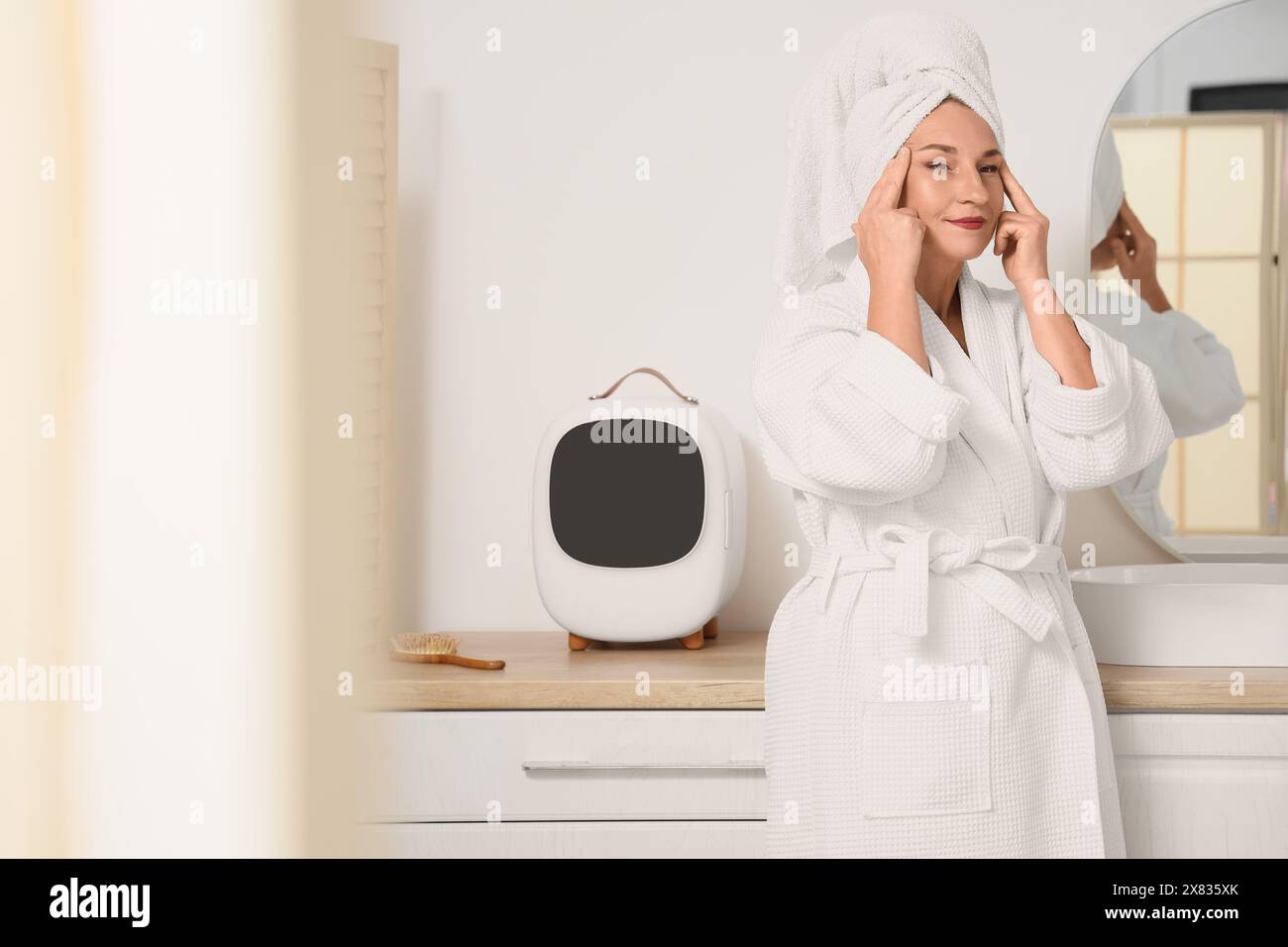 Mature woman doing face building exercise after shower in bathroom ...