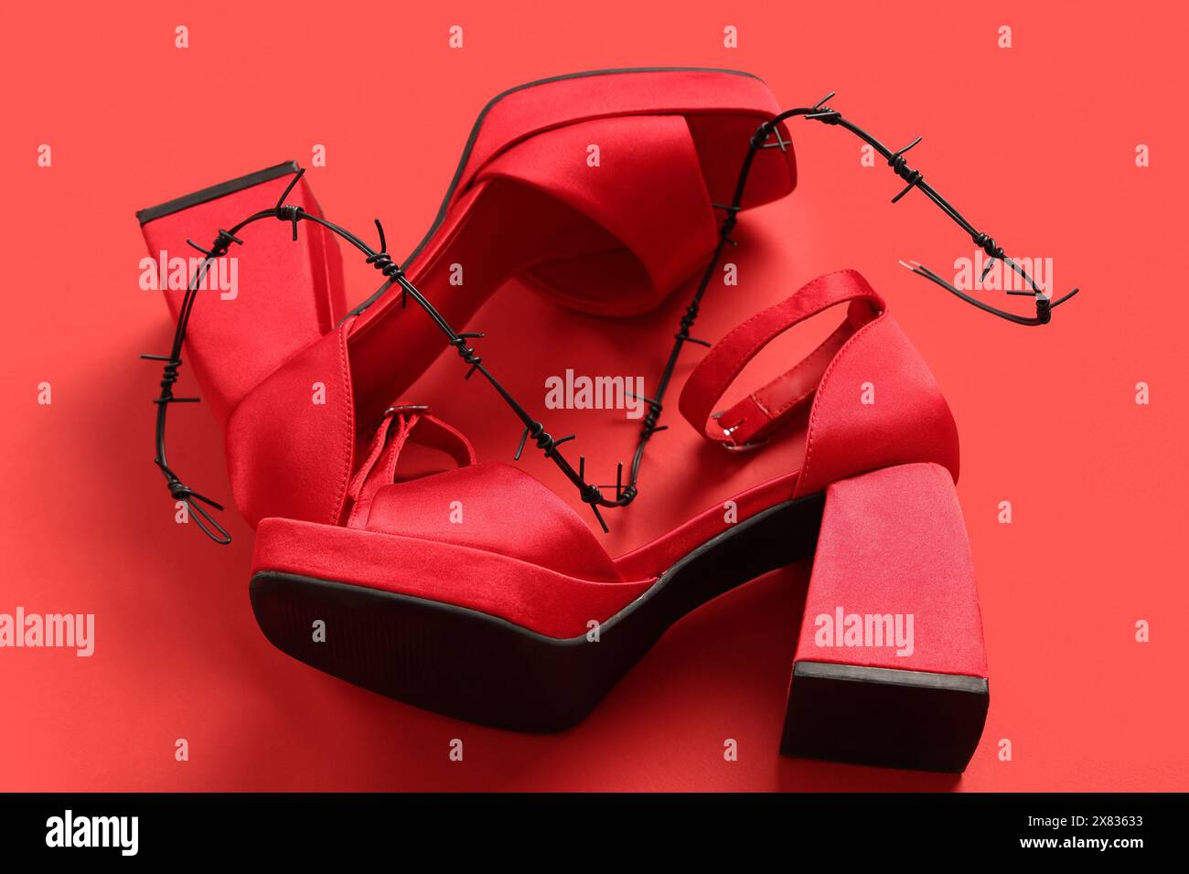 High-heeled shoes wrapped in barbed wire on red background ...