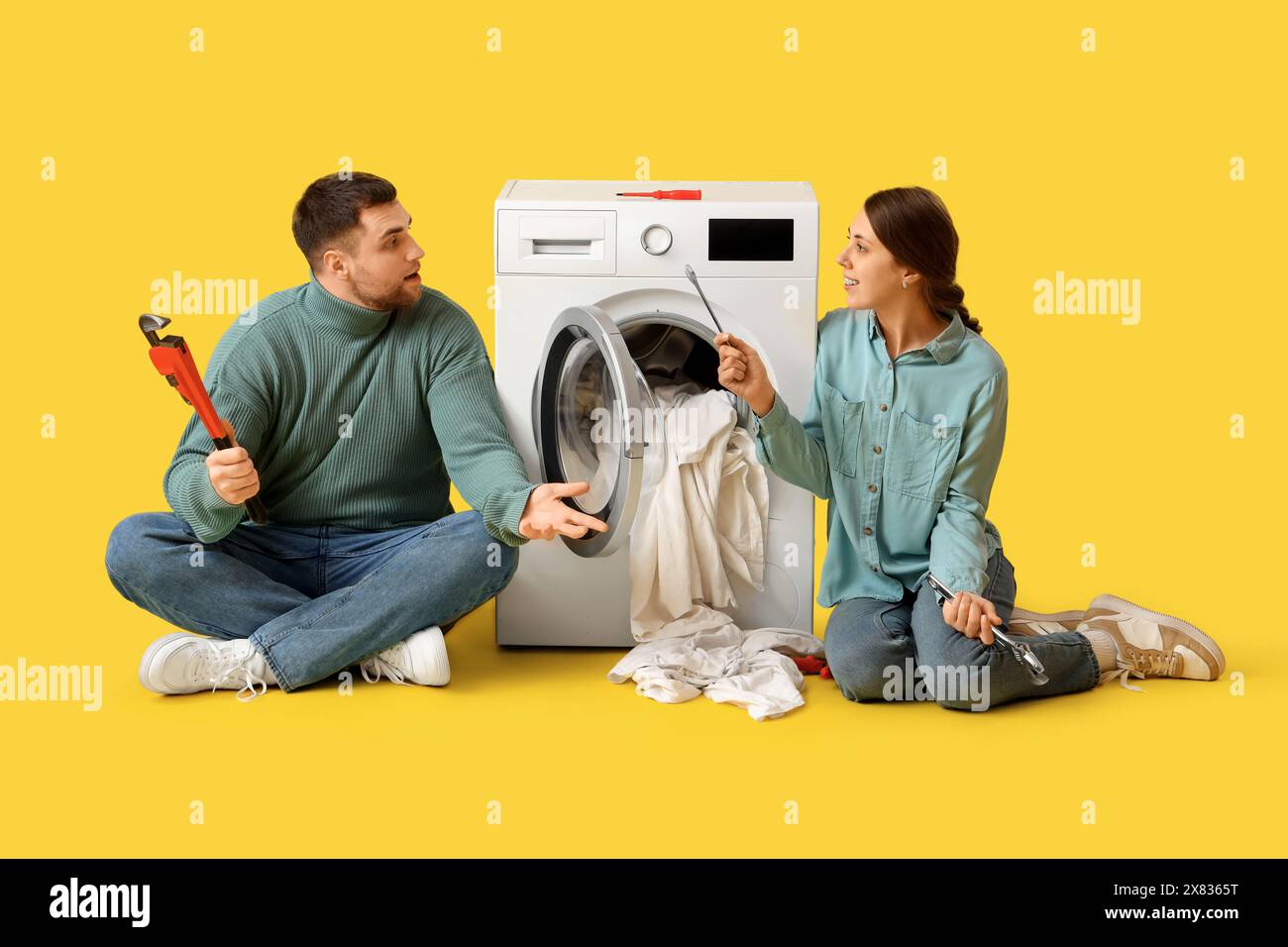 Young couple trying to fix washing machine on yellow background Stock ...