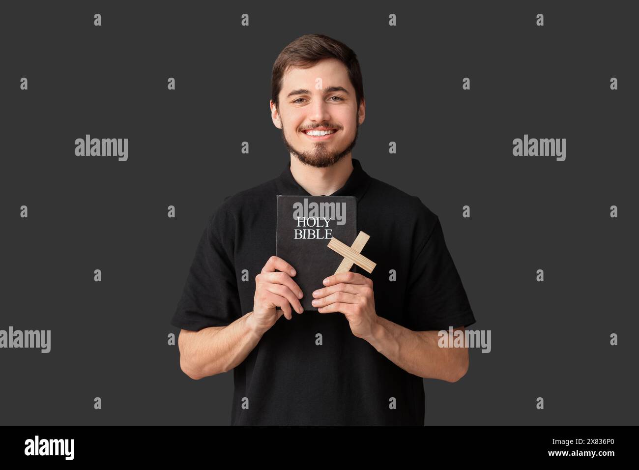 Smiling man with Holy Bible and cross on black background Stock Photo ...