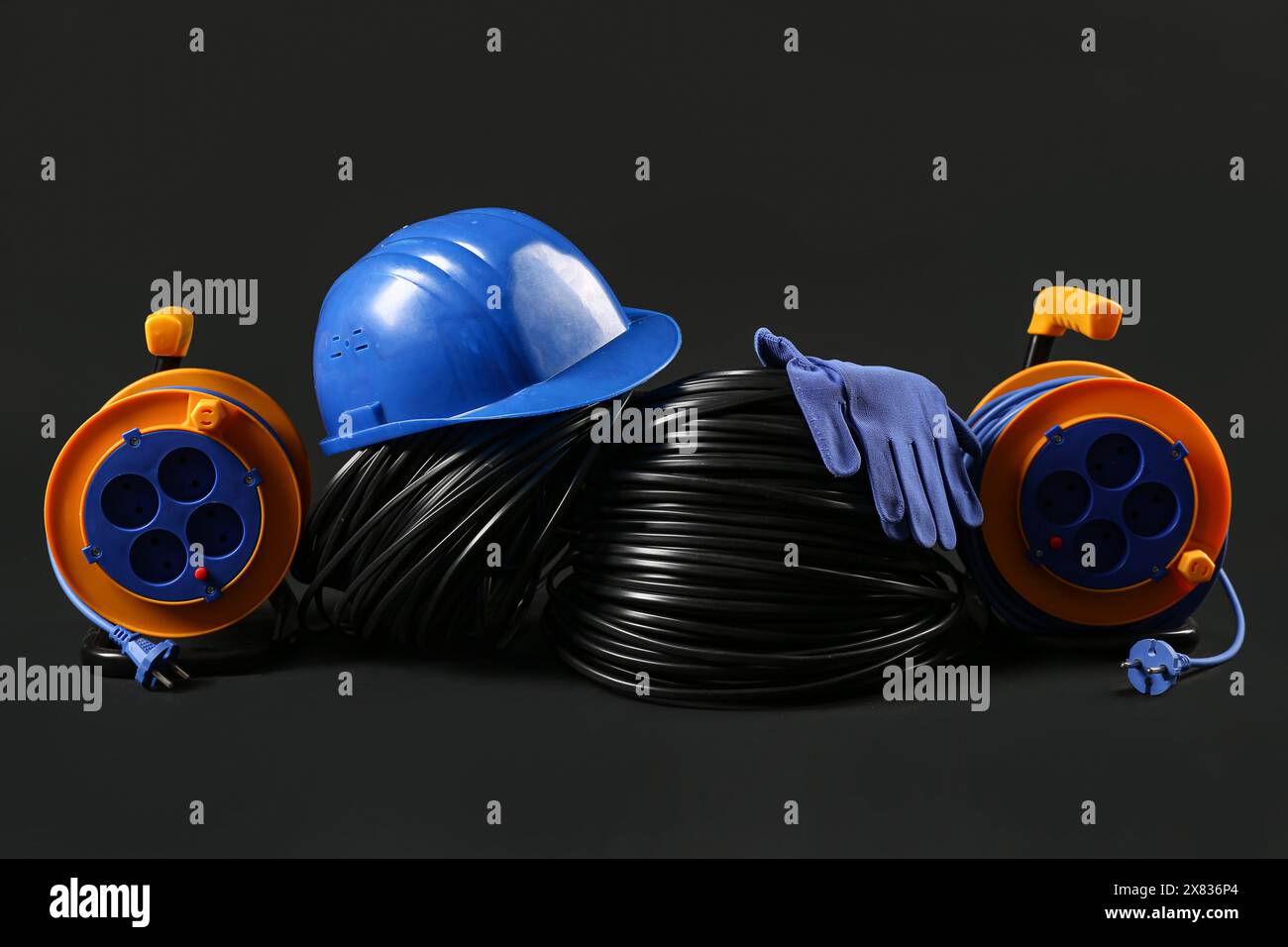 Rolled wires, extension cable reels, hardhat and fabric gloves on black ...