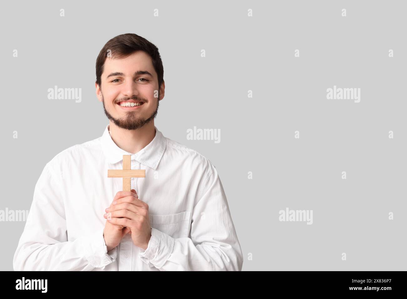 Smiling young man with cross on grey background Stock Photo - Alamy