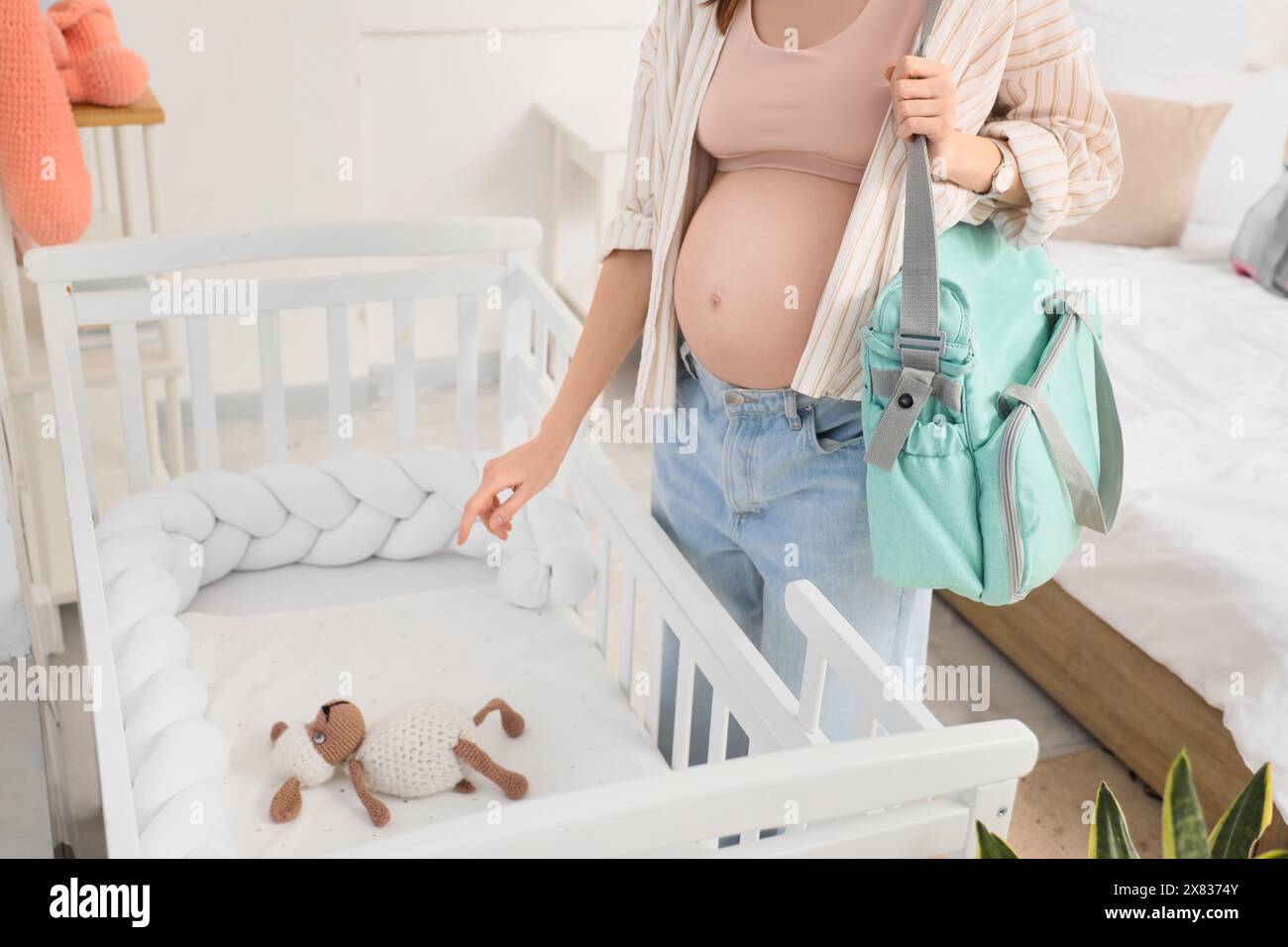 Young pregnant woman with maternity hospital bag near baby crib in ...