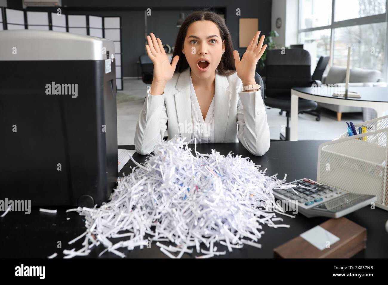 Shocked young secretary with shredded paper and shredder in office ...