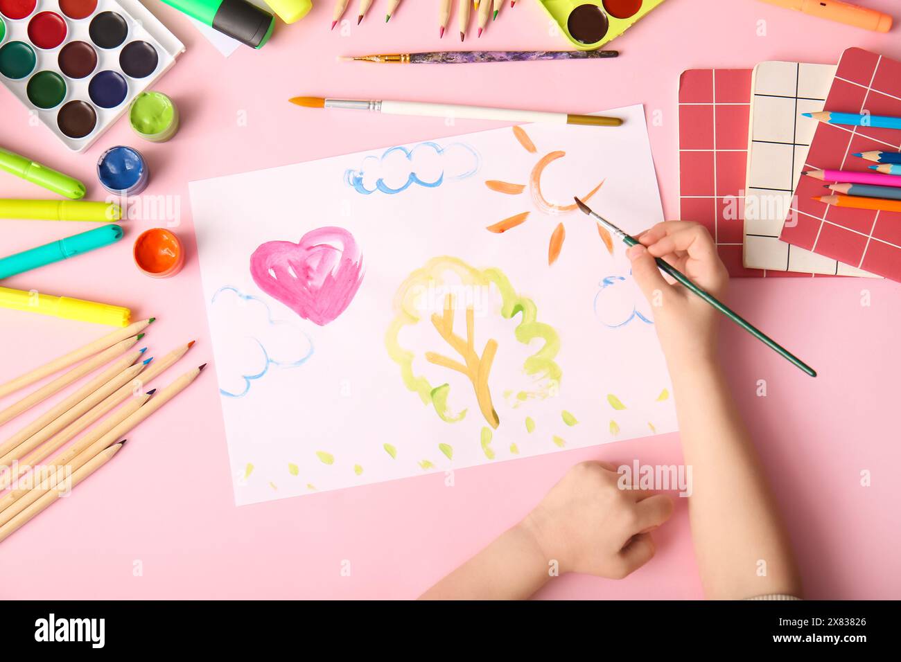 Child's hand drawing tree with brush, paints and pencils on pink ...