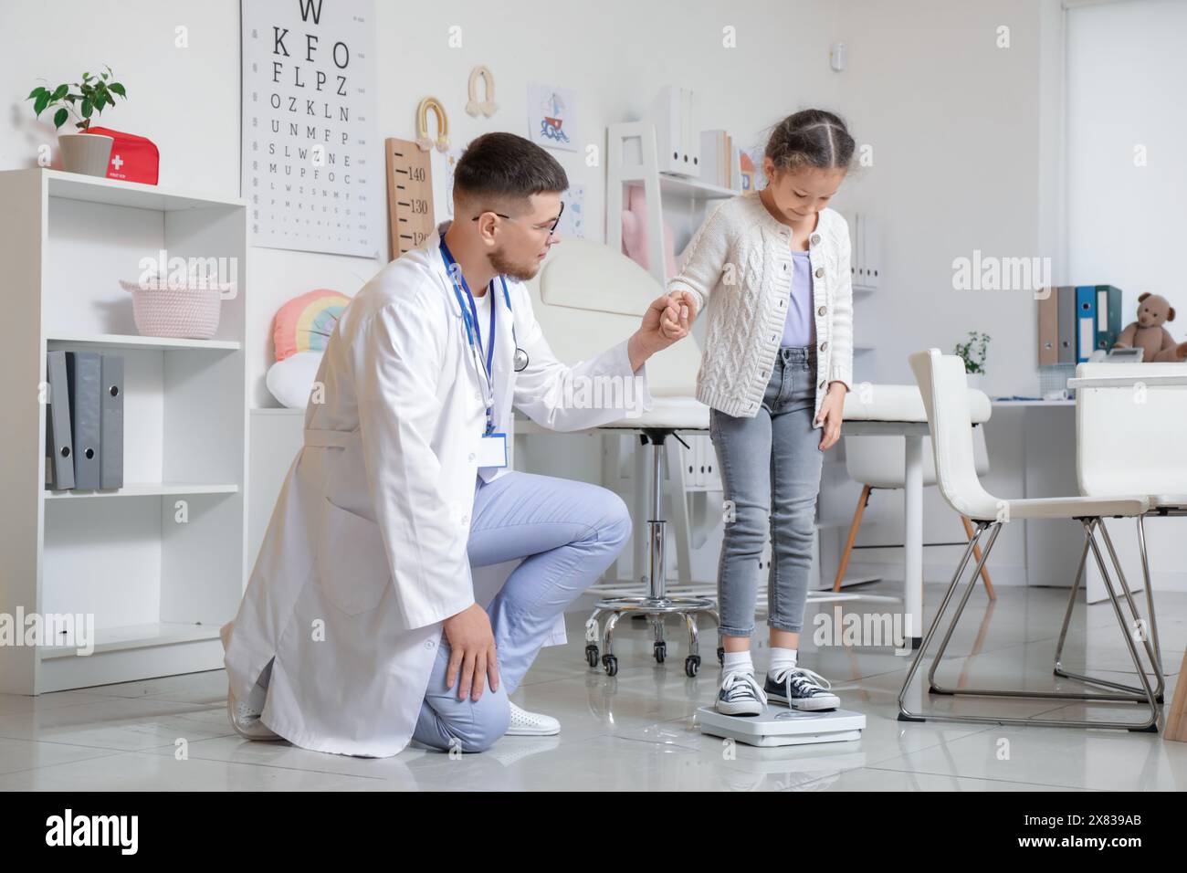 Cute little girl measuring her weight on scales with pediatrician in ...