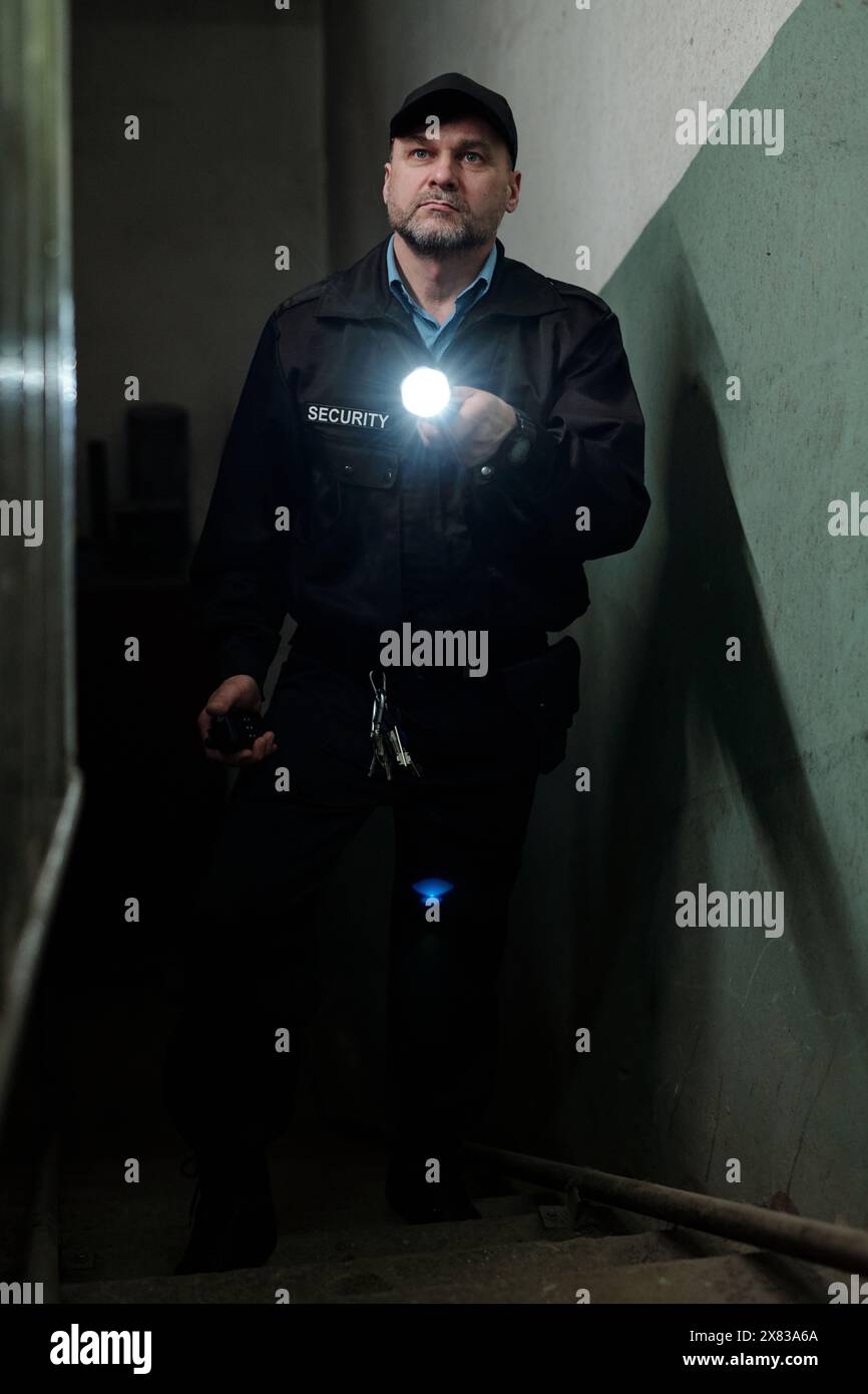 Mature male security guard in black uniform and cap walking upstairs in ...