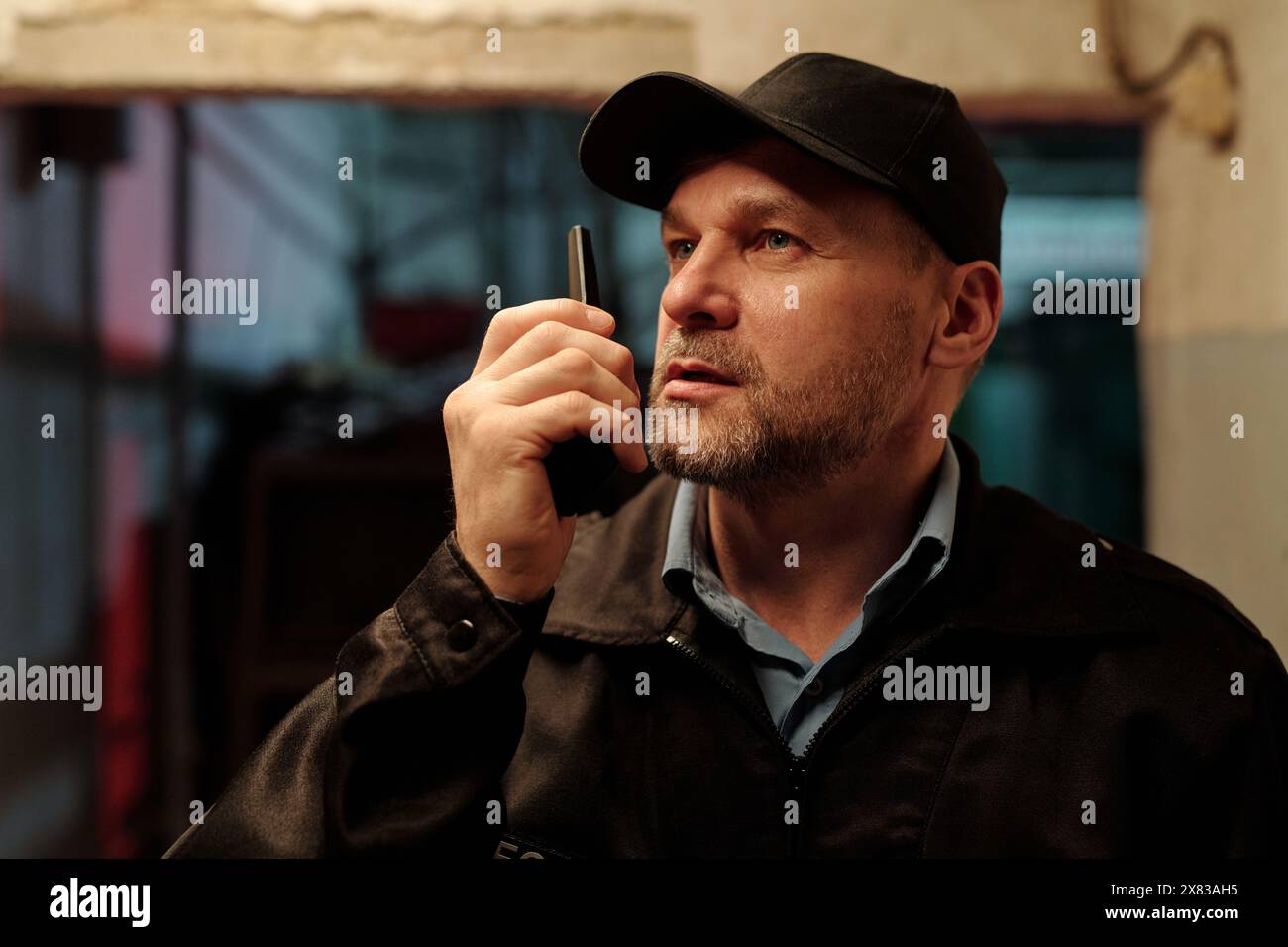 Mature male security staff in cap and black uniform standing in front ...