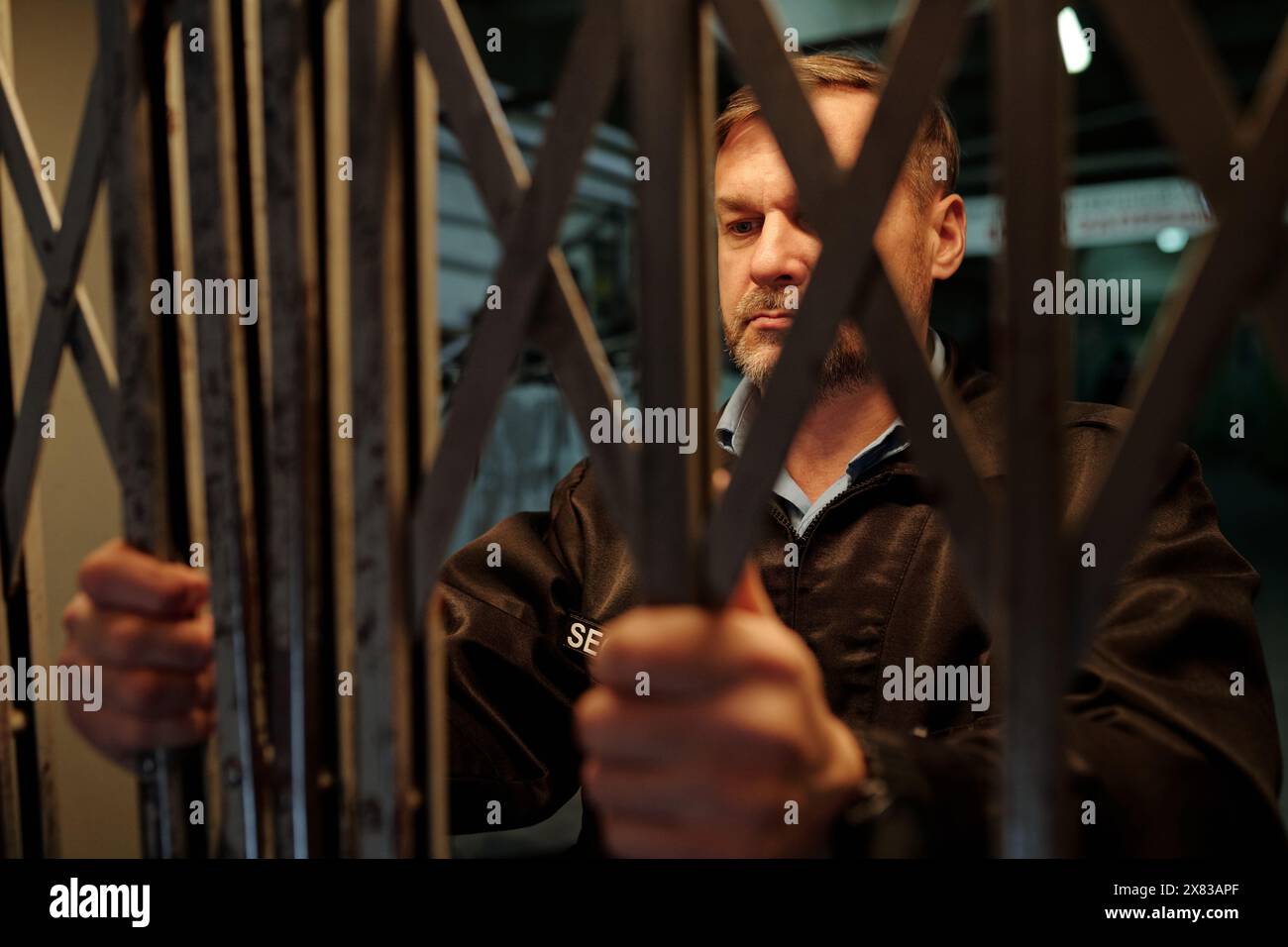 Serious mature male guard standing behind mesh and opening gate before ...