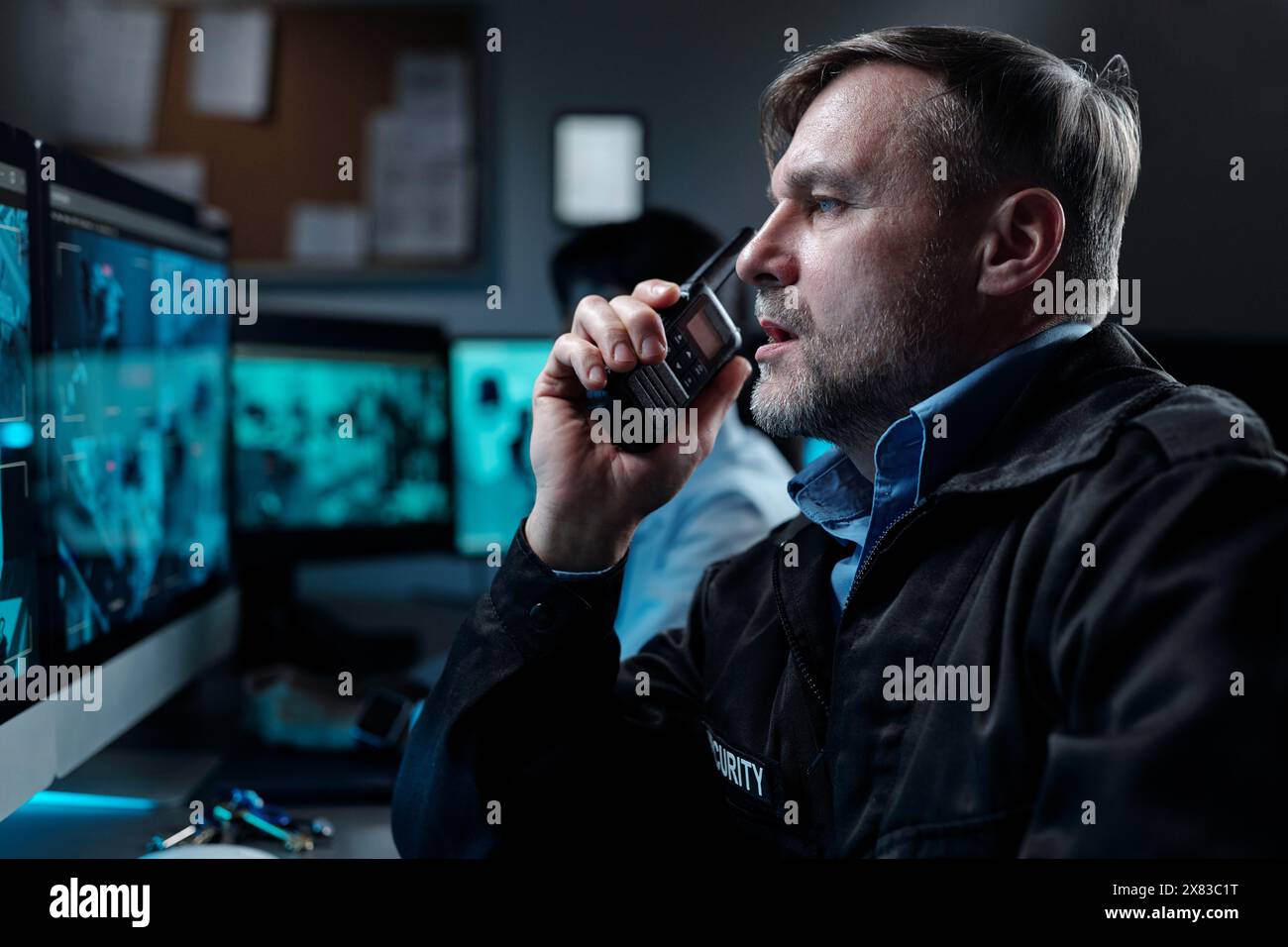 Mature male security guard with walkie-talkie by mouth reporting ...