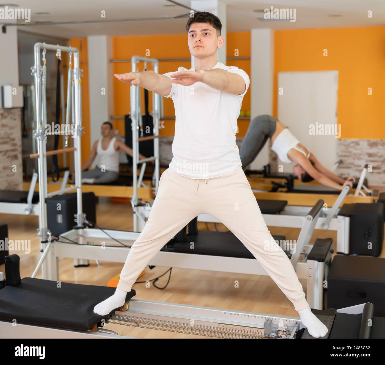 Guy performing exercises on Pilates reformer to stretch body muscles ...