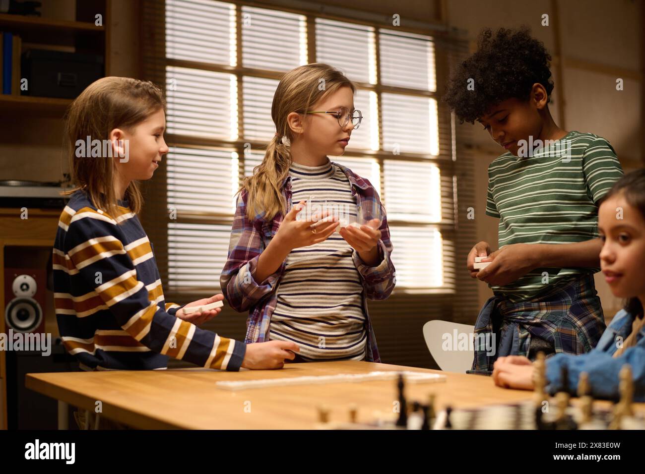 Youthful boy and girl looking at cute African American boy with domino ...