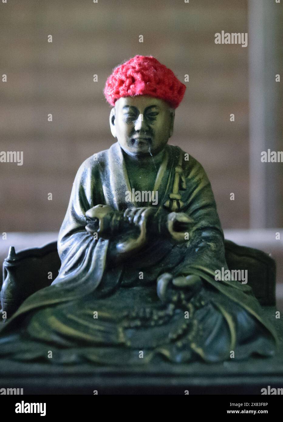 A statue of a seated monk wearing a red knitted hat. The monk is ...