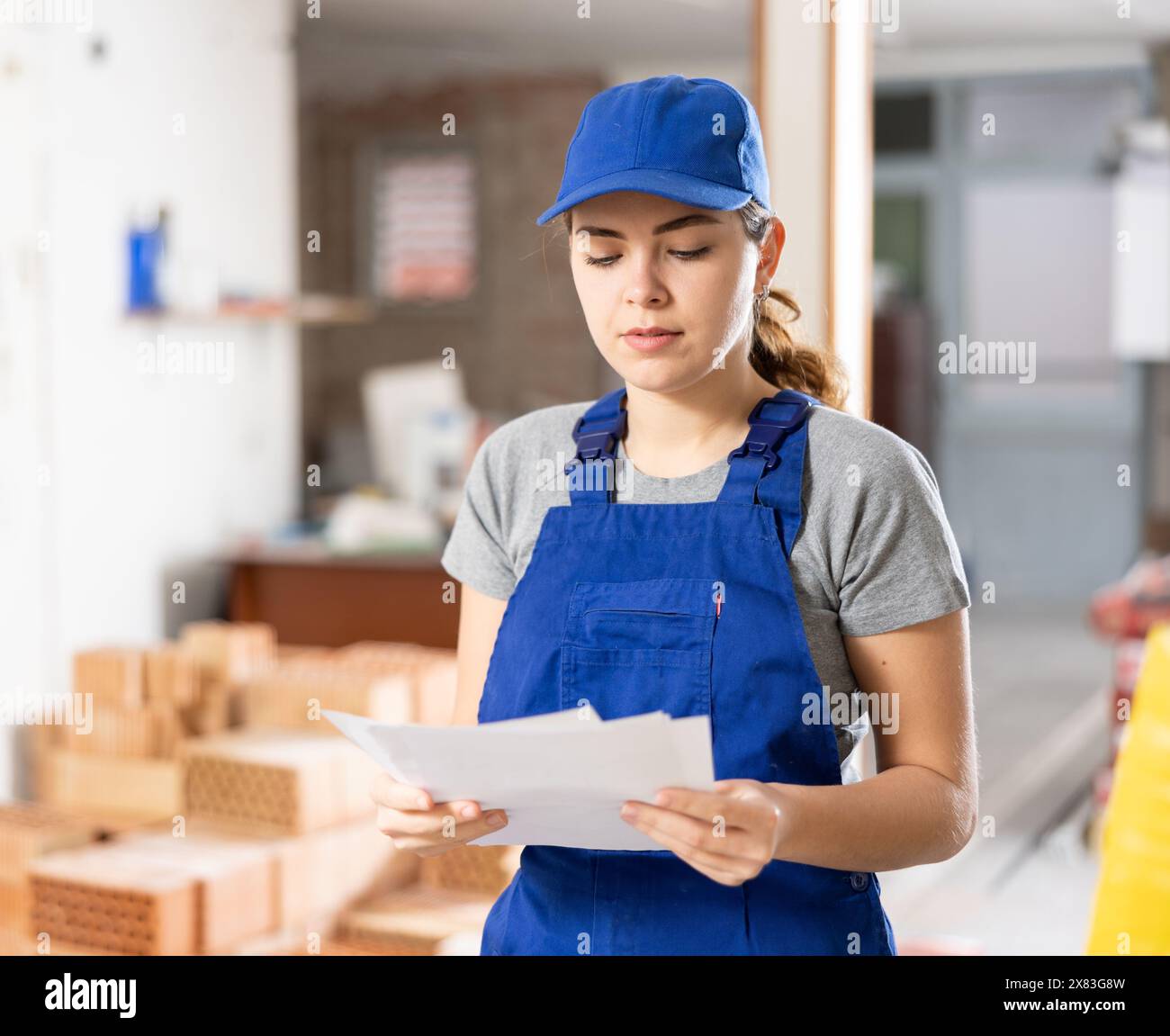 Female designer in blue overalls with papers planning building overhaul ...