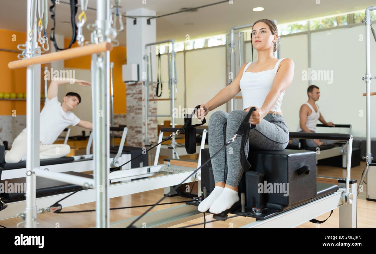 Girl in gym with help of rope reformer performs exercises to strengthen ...