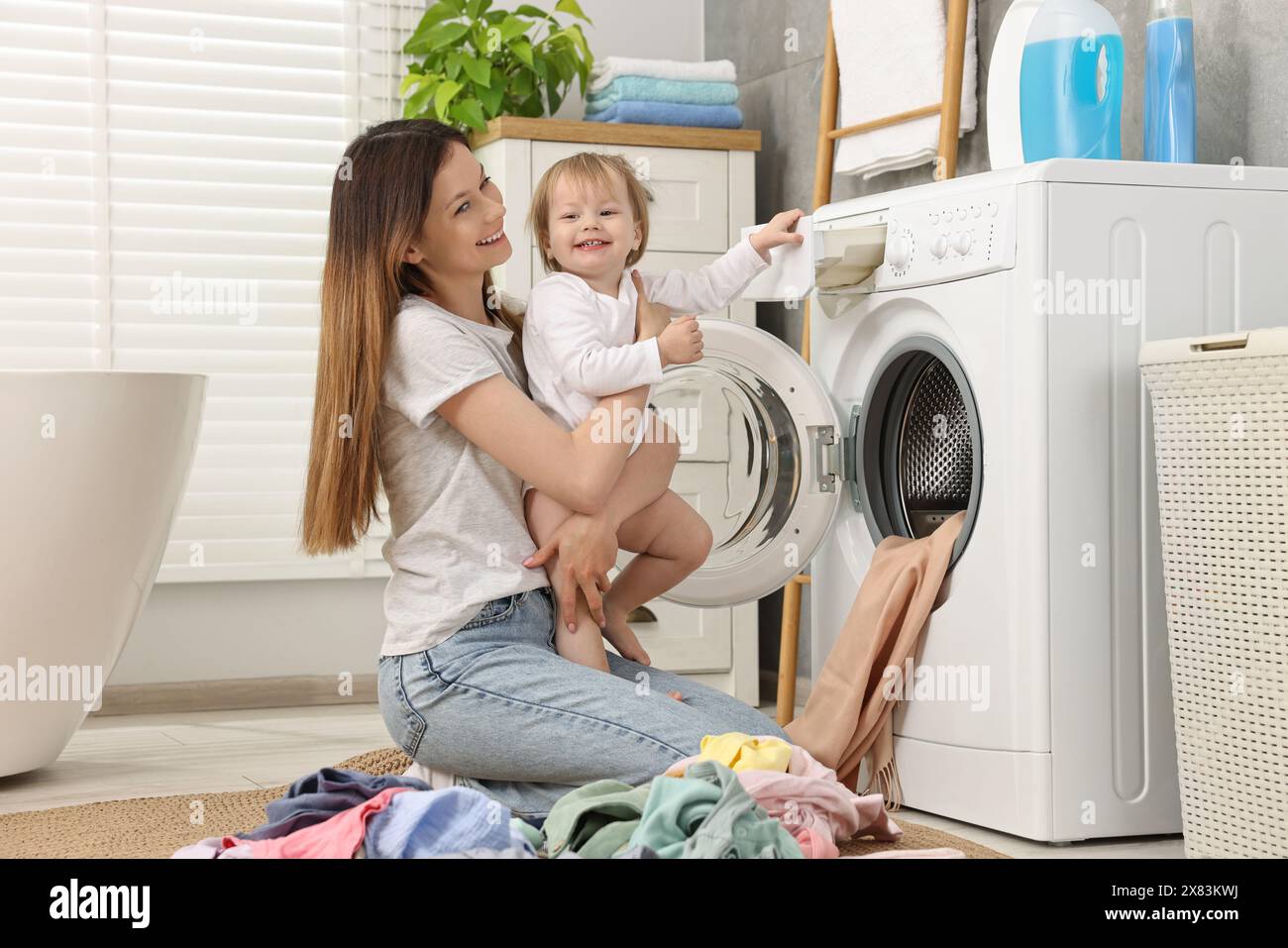 Happy mother with her daughter having fun while washing baby clothes in ...