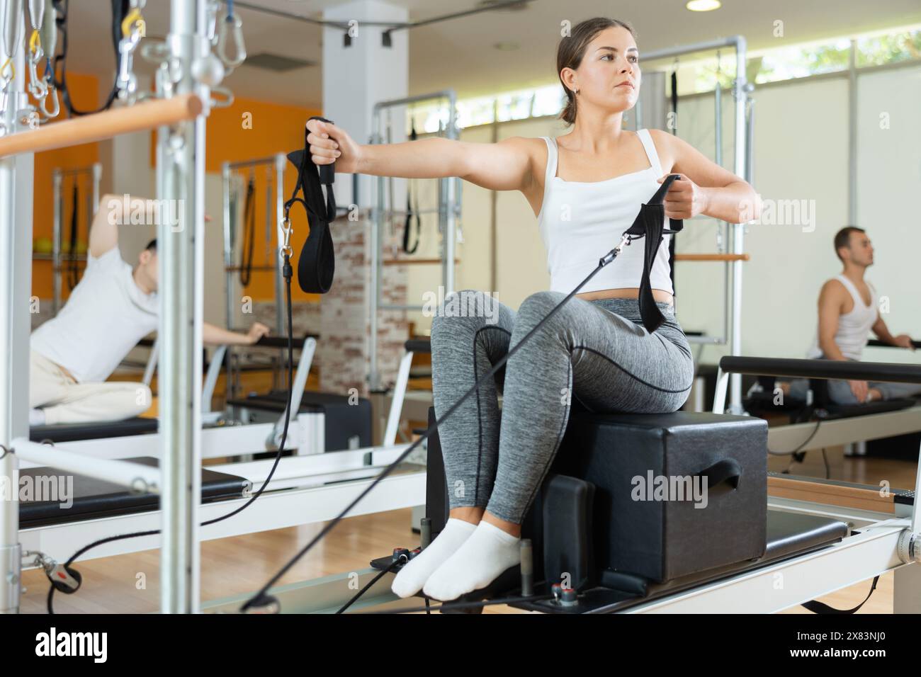 Girl in gym with help of rope reformer performs exercises to strengthen ...