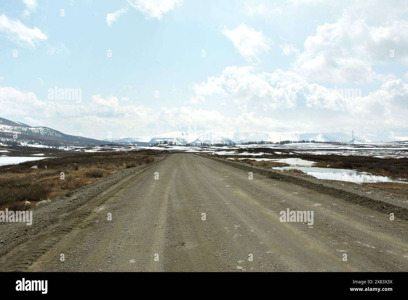 A muddy gravel road crosses a huge snow covered clearing surrounded by ...