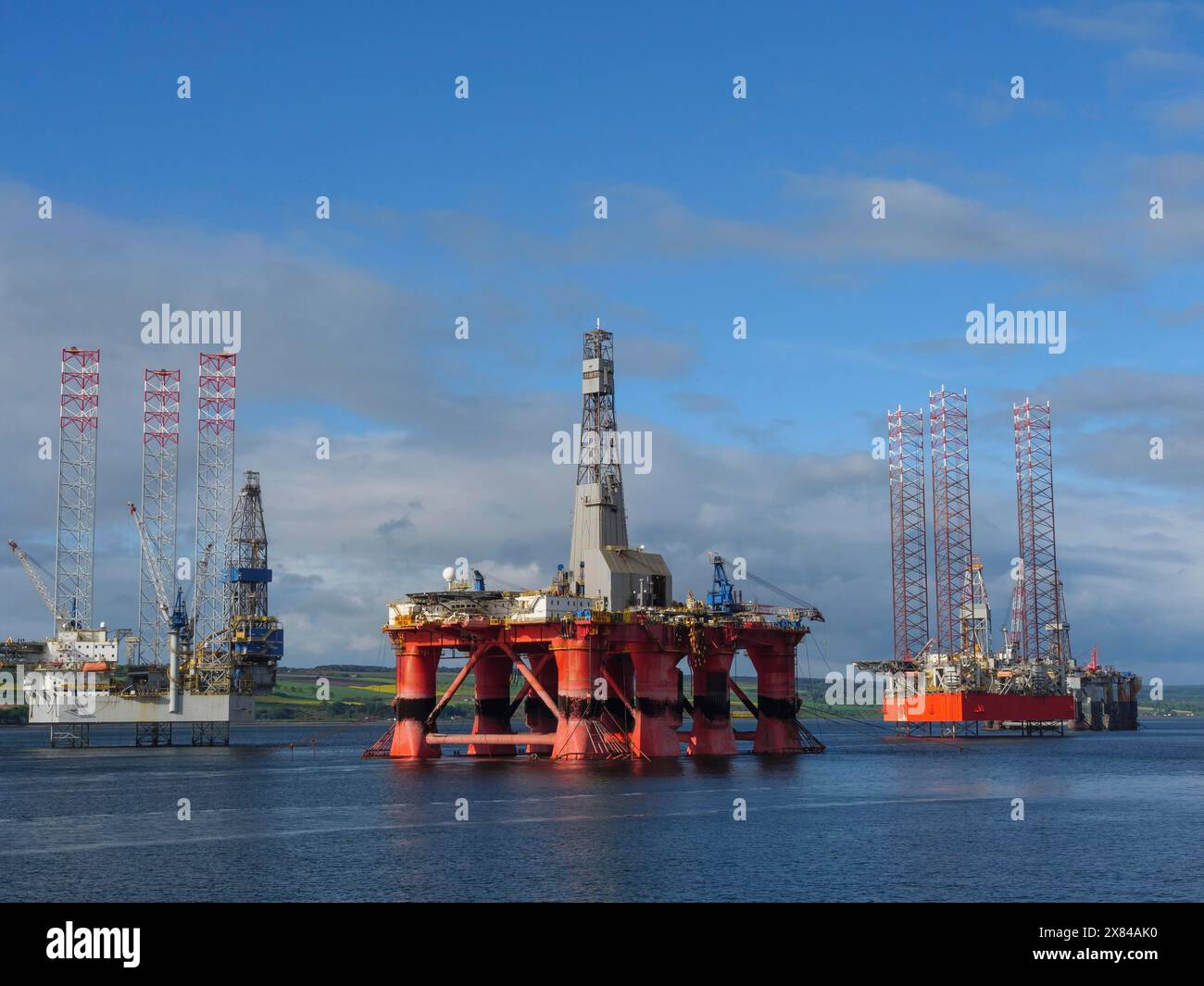Three oil rigs standing side by side in a calm sea under a blue sky ...