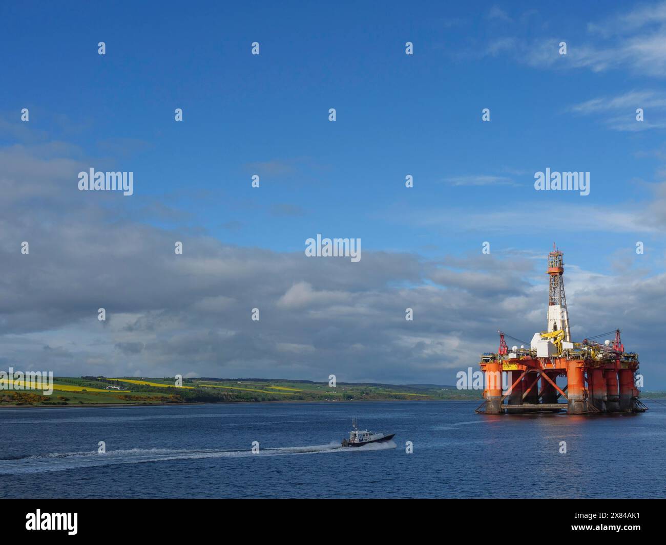 An oil drilling platform stands in the calm sea, a small boat sails in ...