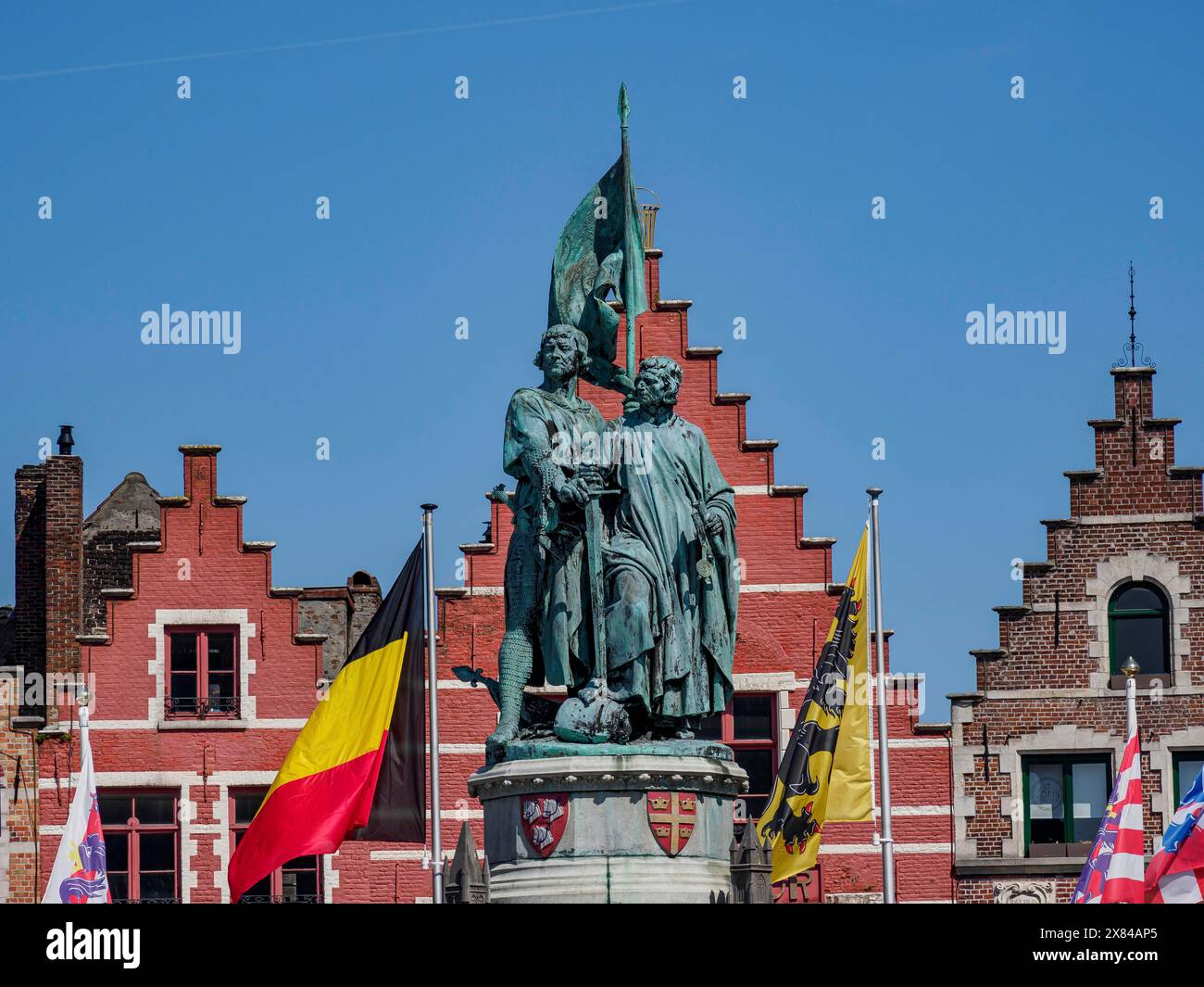 A statue in front of traditional Belgian brick buildings and flags in ...