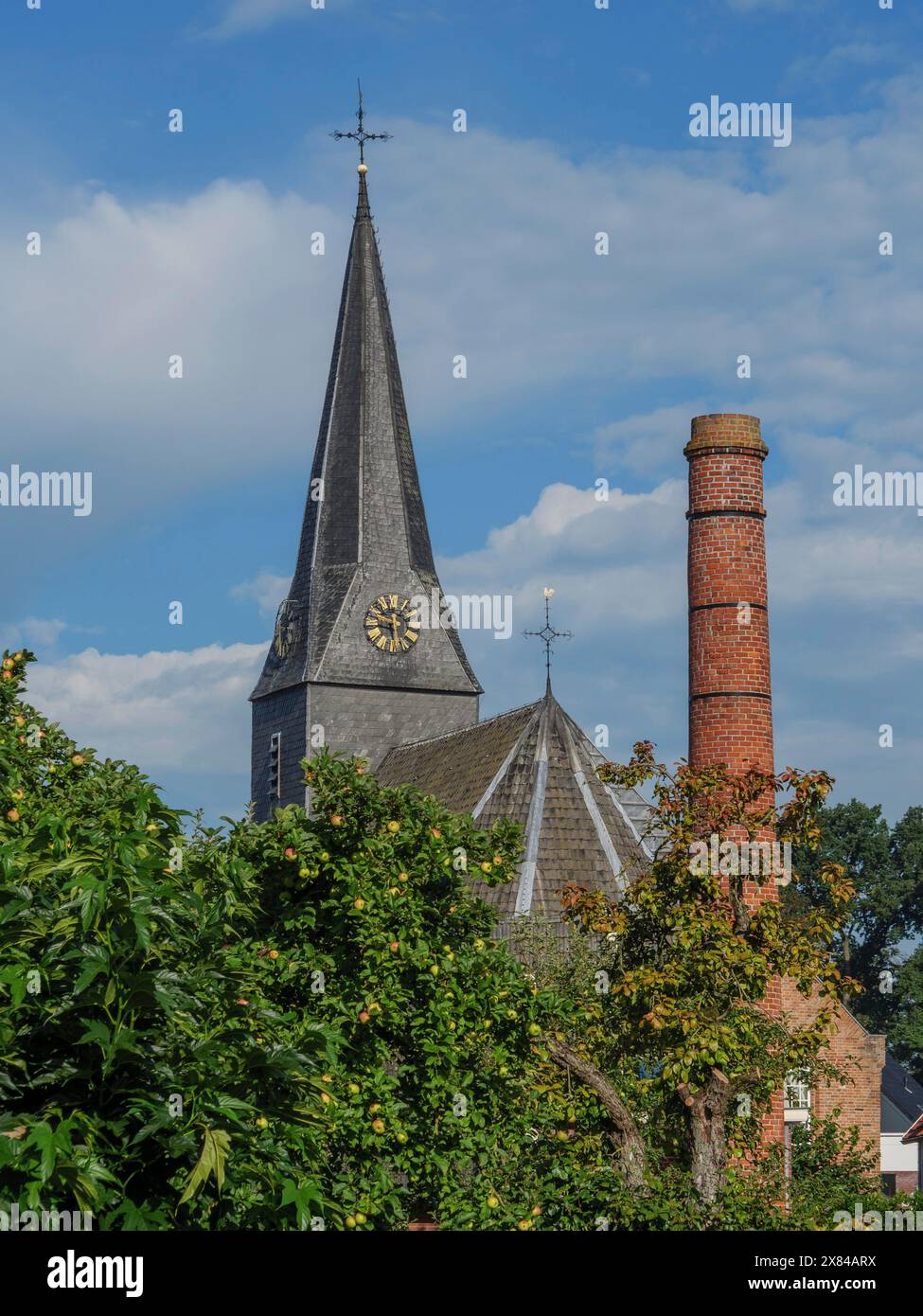 Church tower and chimney, surrounded by trees, in sunny weather with ...
