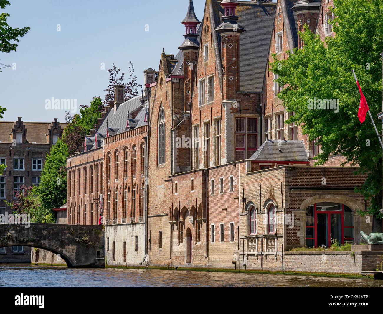 Brick-coloured buildings and stone bridge along a canal with summer ...